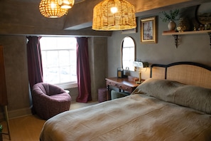 Quarto com cama grande, escrivaninha, cadeira, cômoda e janela com cortinas.