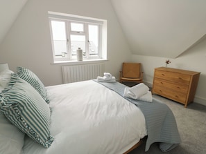 Quarto com cama, cadeira, penteadeira e janela.