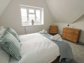Quarto com cama, cadeira, penteadeira e janela.