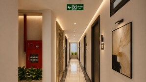 Corredor de hotel com carretel de mangueira de incêndio, sinal de saída e uma obra de arte emoldurada na parede.