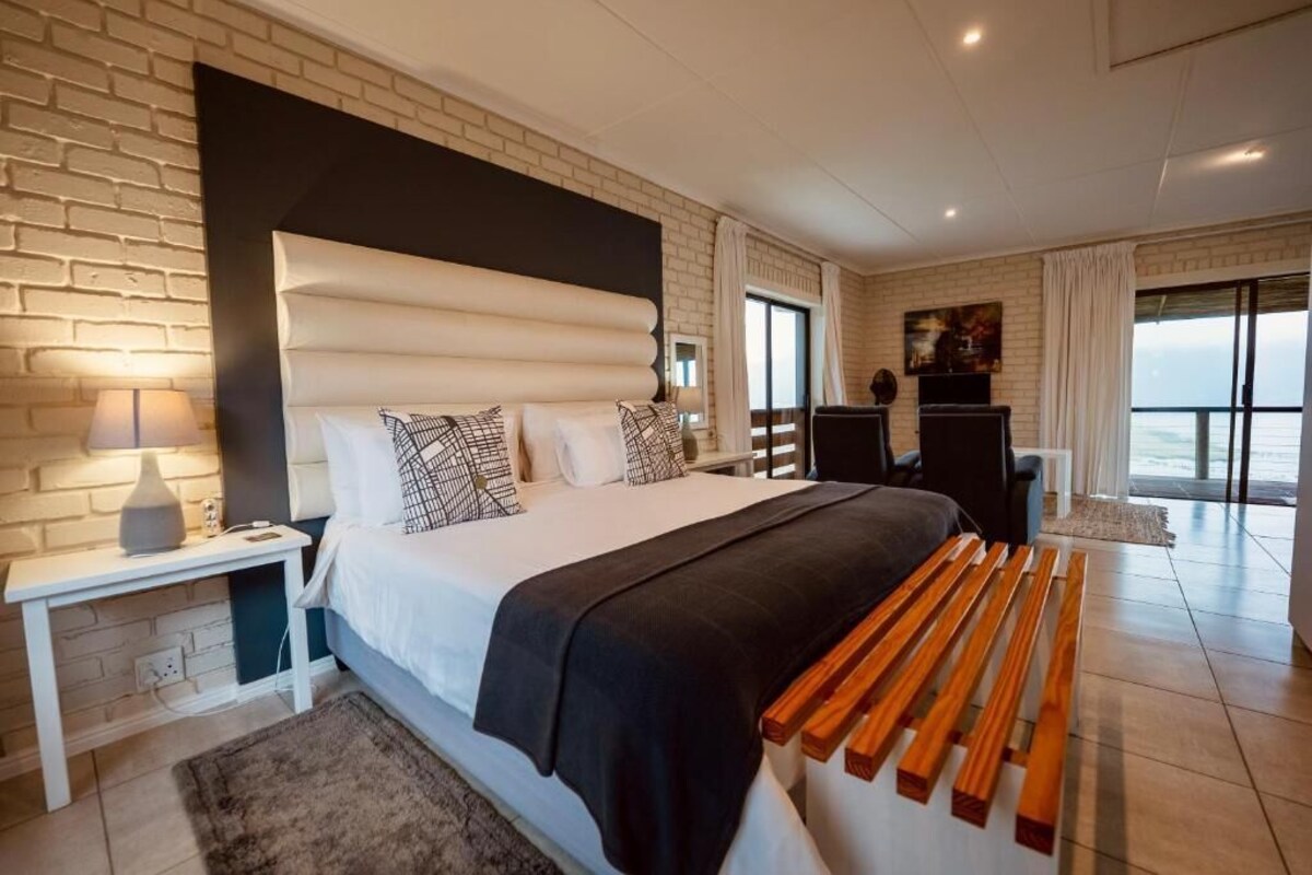 Quarto moderno com uma cama grande, mesa de cabeceira, escrivaninha e vista para o mar.