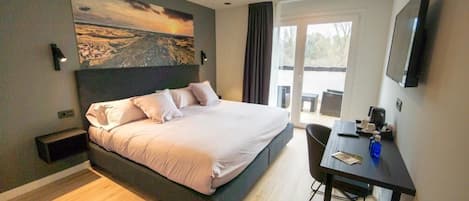 Quarto de hotel moderno com uma cama, escrivaninha, cadeira, televisão de tela plana e uma janela grande.