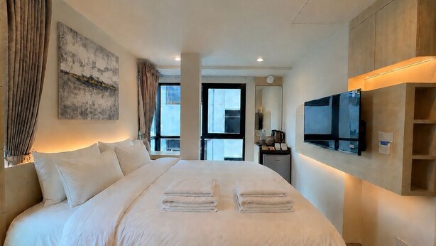 Quarto de hotel moderno com uma cama grande, televisão de tela plana na parede e uma pequena área de cozinha.