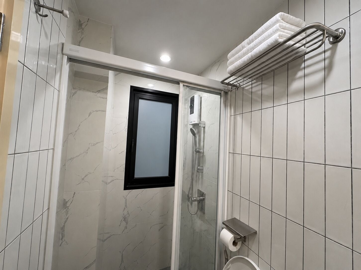 Casa de banho com chuveiro em cabine de vidro, sanita, porta-toalhas e parede revestida a mármore.