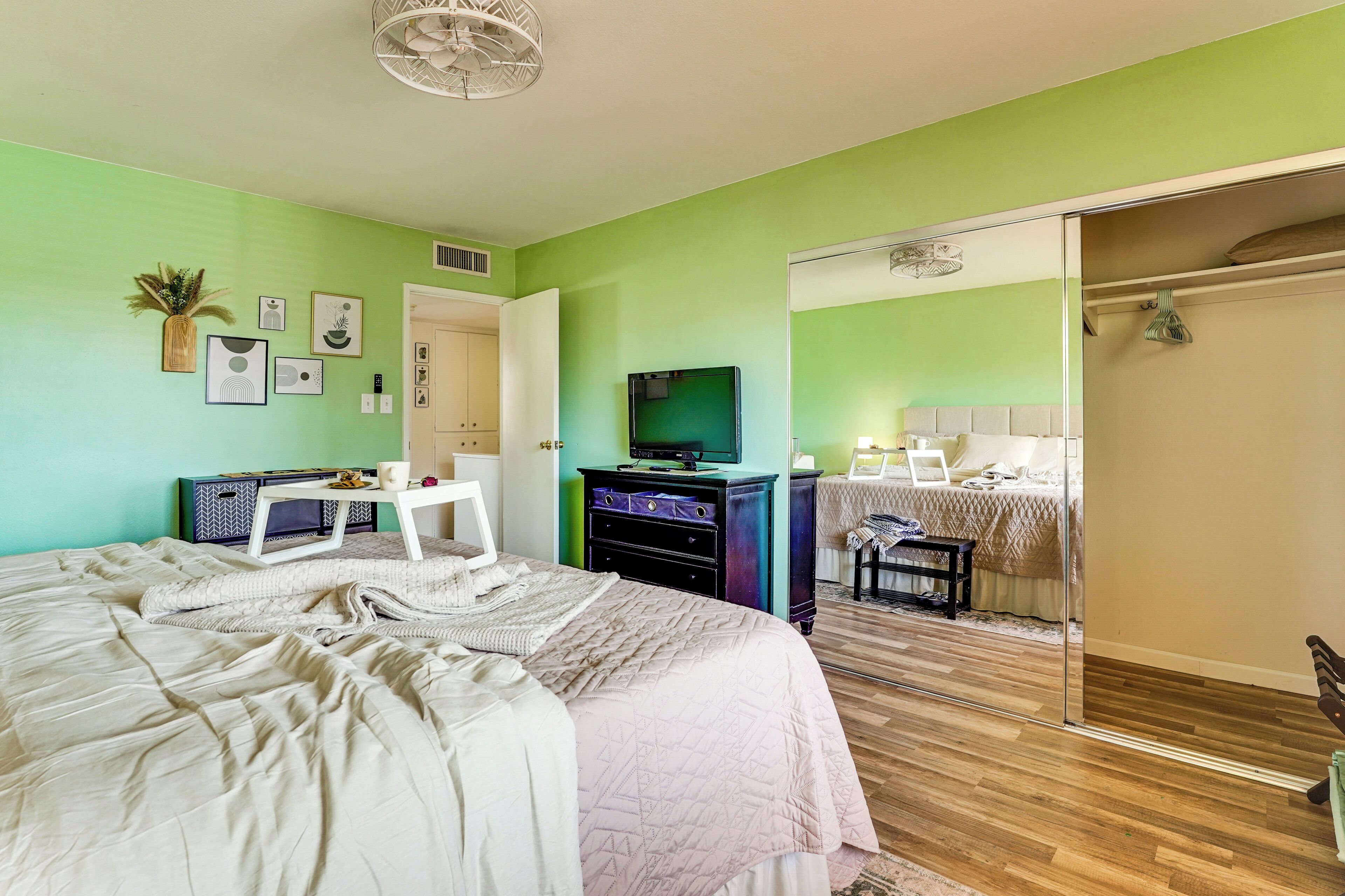 Quarto com cama, escrivaninha, televisão e espelho.