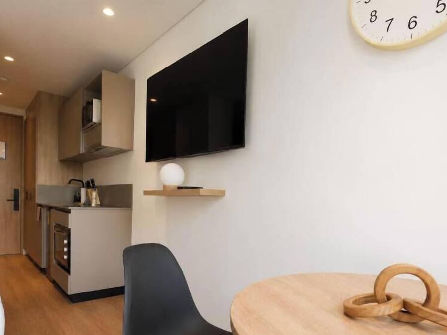 Cozinha compacta com televisão de tela plana, uma mesa de madeira com um anel e um relógio na parede.