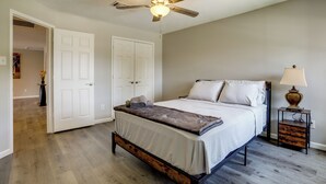 Quarto com cama, ventoinha no teto, mesa de cabeceira e abajur.