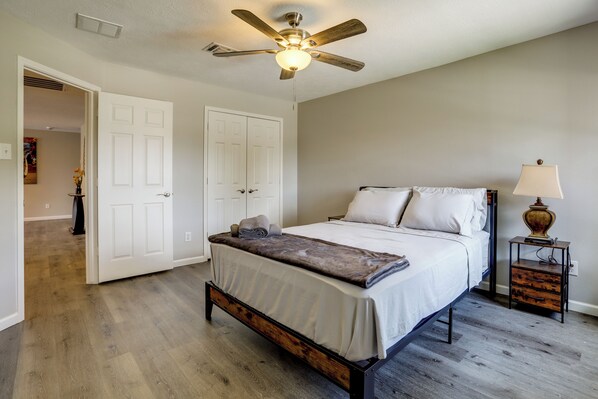Quarto com cama, ventoinha no teto, mesa de cabeceira e abajur.