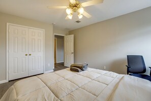 Quarto com cama, ventoinha no teto, cadeira e porta.