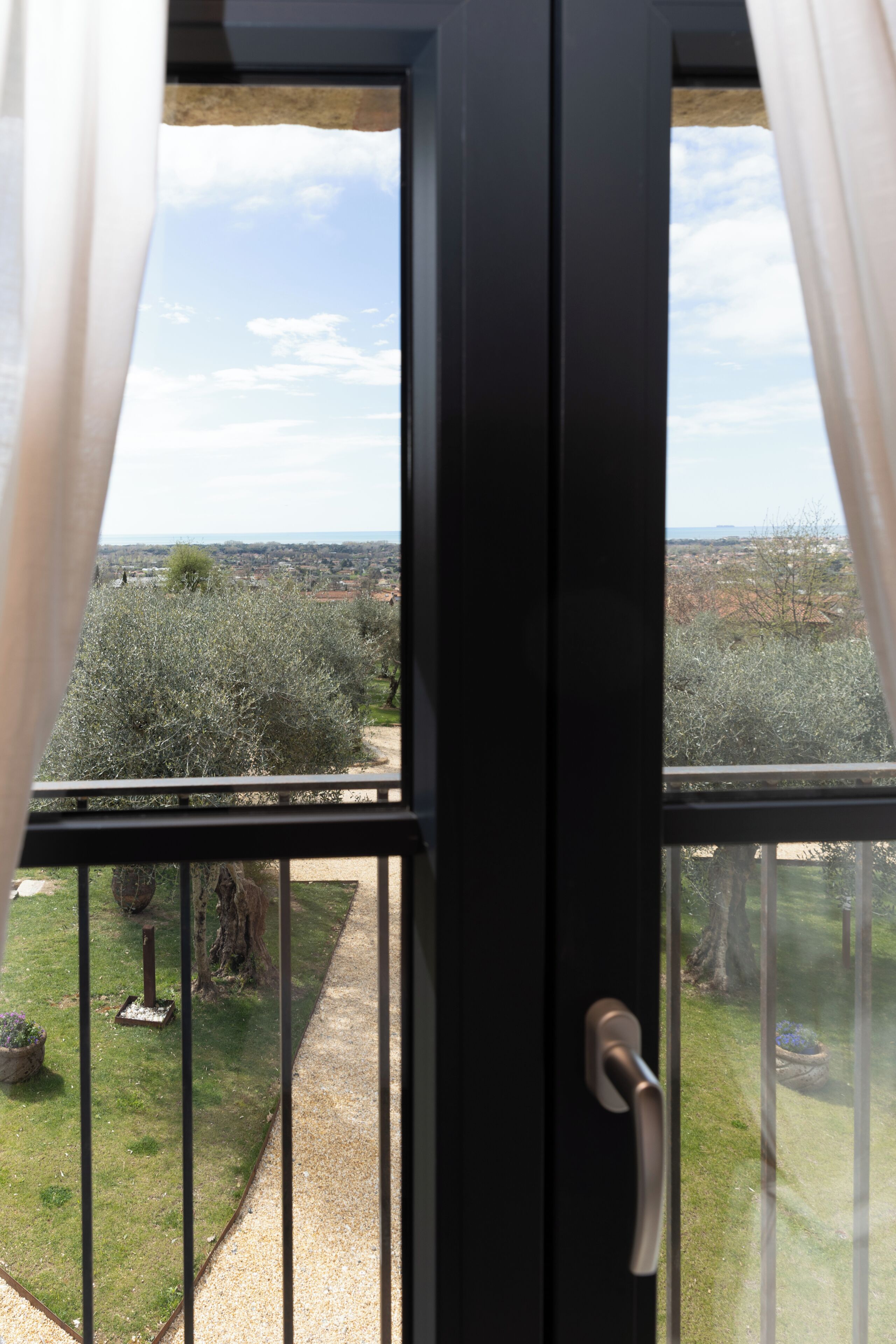 Vista pela janela, com uma porta, varanda e área gramada com árvores.