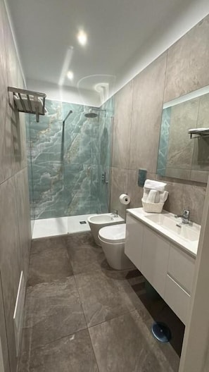 Uma casa de banho moderna com chuveiro em cabine de vidro, sanita e lavatório com espelho em cima.