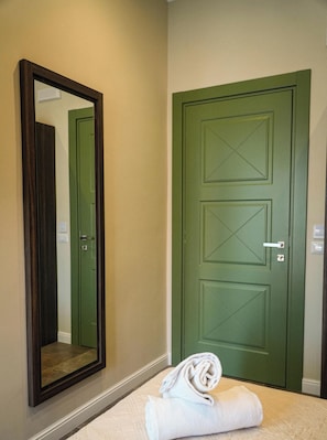 Um quarto com porta verde, um espelho e uma toalha enrolada na cama.