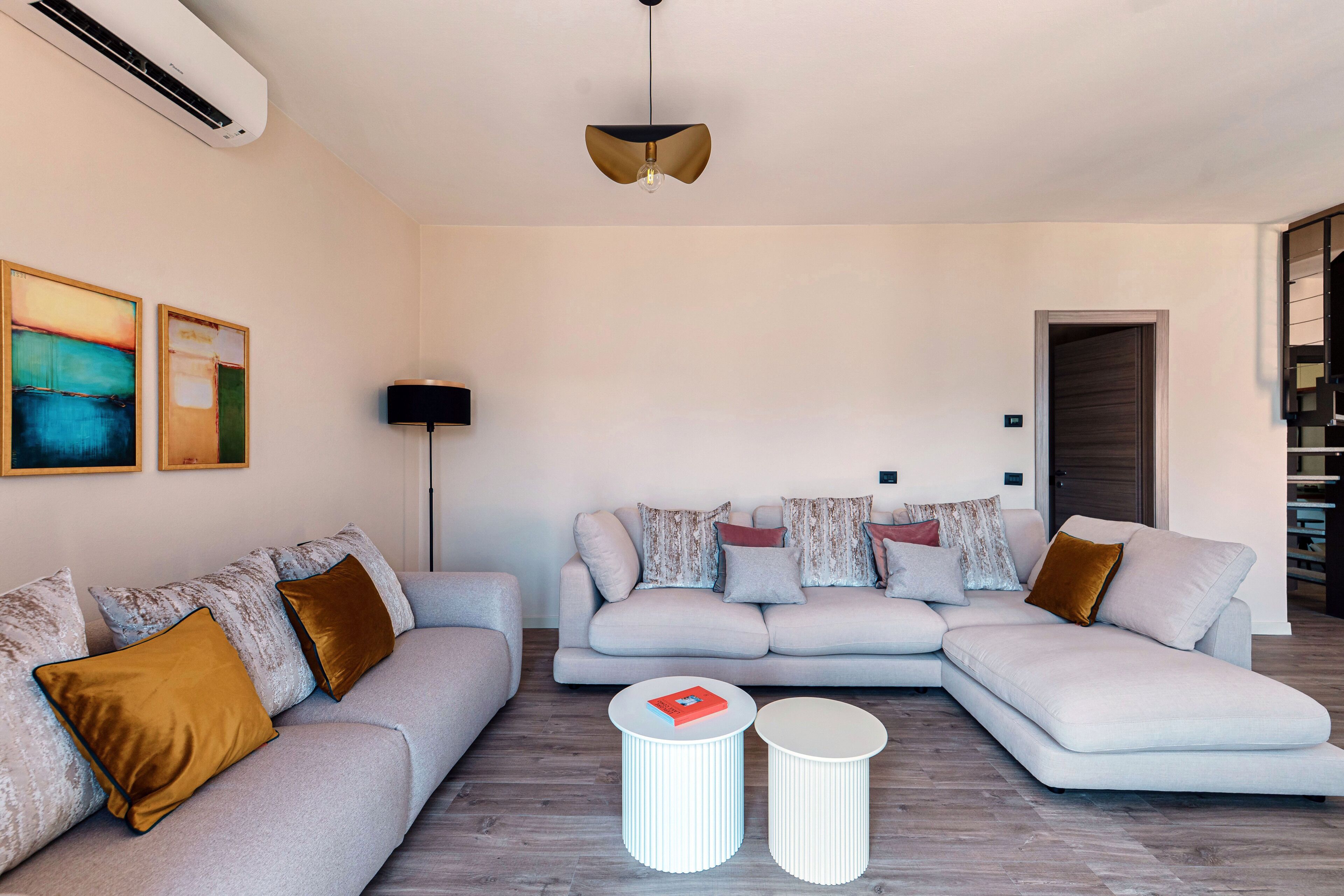 Uma sala de estar moderna com um sofá seccional, duas mesas laterais e uma luminária pendente.