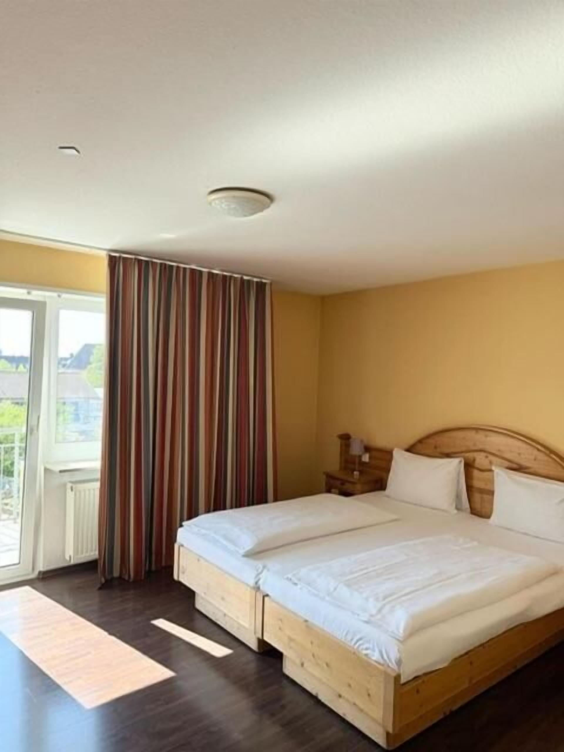 Uma cama de casal com cabeceira de madeira, mesa de cabeceira e janela com cortinas.
