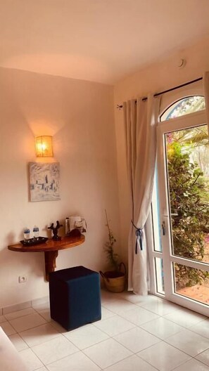 Quarto com janela, luminária fixada na parede, uma mesinha com objetos e um vaso de planta.