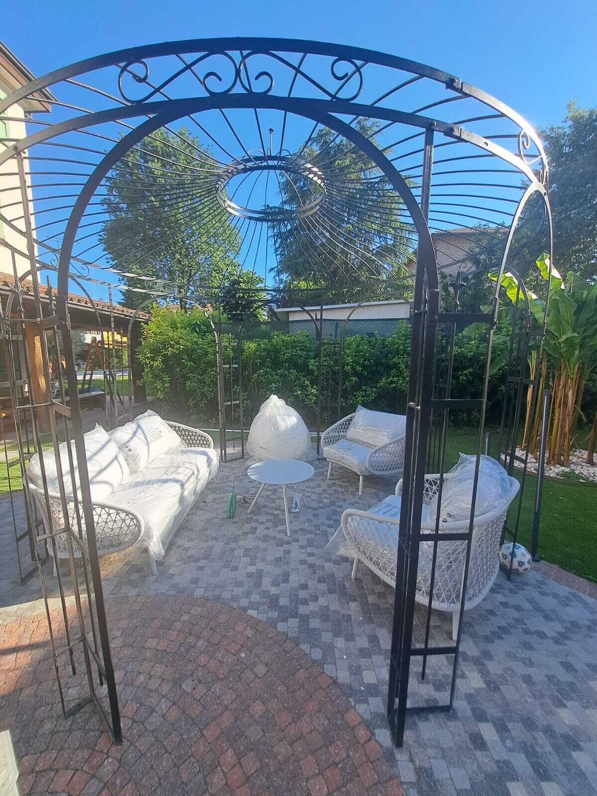 Uma área de estar coberta ao ar livre com estrutura de pérgola, mobiliário de vime e um pátio pavimentado.