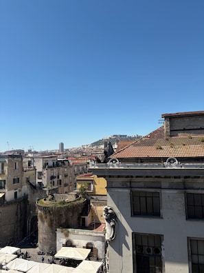 Paisagem urbana com edifícios históricos, céu claro e vista da cidade ao longe.