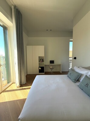 Quarto de hotel moderno com uma cama grande, uma escrivaninha e vista para a cidade.