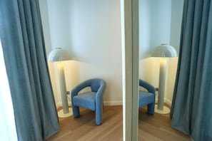 Um quarto com uma poltrona azul, duas luminárias de chão e cortinas cinzas.
