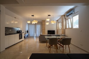 Cozinha moderna com armários brancos, forno embutido e micro-ondas. Há uma área de refeições com mesa de vidro e cadeiras.
