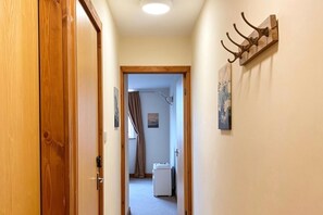 Um corredor com uma porta de madeira, um cabide e uma máquina de lavar ao fundo.