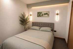 Quarto com cama, mesa de cabeceira, luminária na parede e planta.