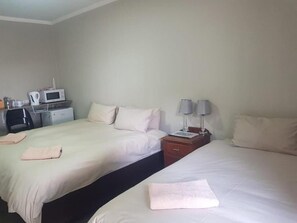Quarto de hotel com duas camas, uma mesa com micro-ondas, uma lâmpada e uma cadeira.