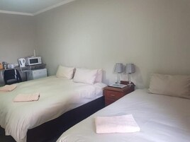 Quarto de hotel com duas camas, uma mesa com micro-ondas, uma lâmpada e uma cadeira.
