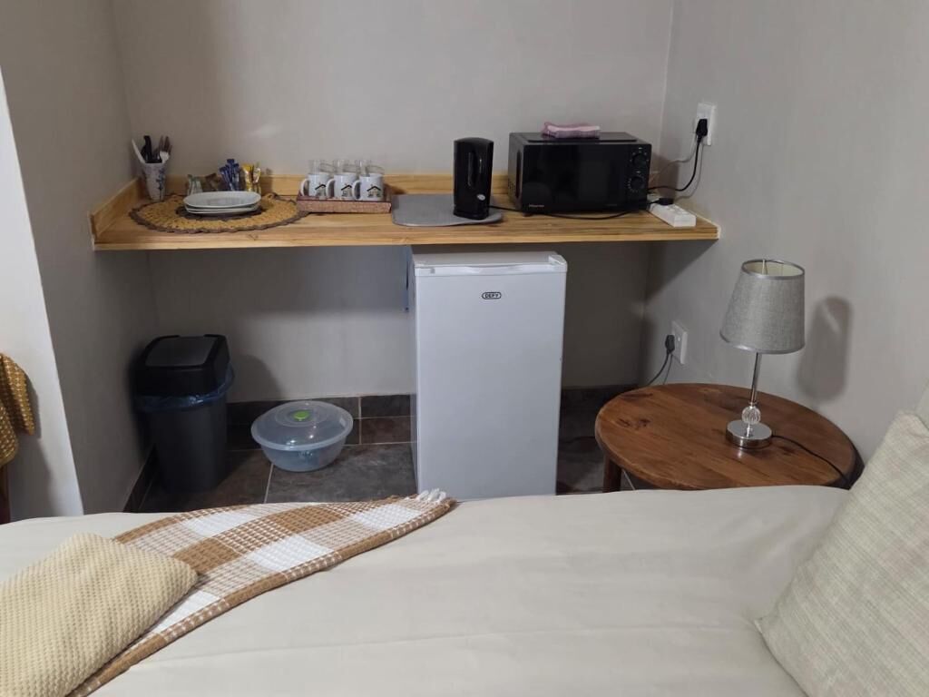 Quarto de hotel compacto com uma cama, uma pequena mesa com micro-ondas, geladeira, lixeira e abajur.