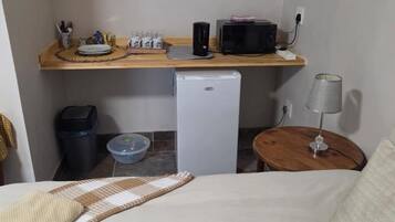 Quarto de hotel compacto com uma cama, uma pequena mesa com micro-ondas, geladeira, lixeira e abajur.