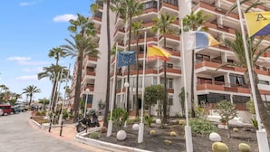 Um hotel de vários andares com varandas, palmeiras e bandeiras.