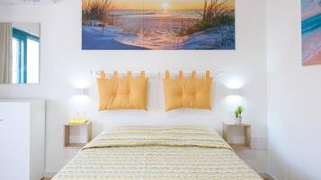 Um quarto com uma cama, duas mesas de cabeceira, um criado-mudo, uma luminária na parede e um quadro sobre a cama.