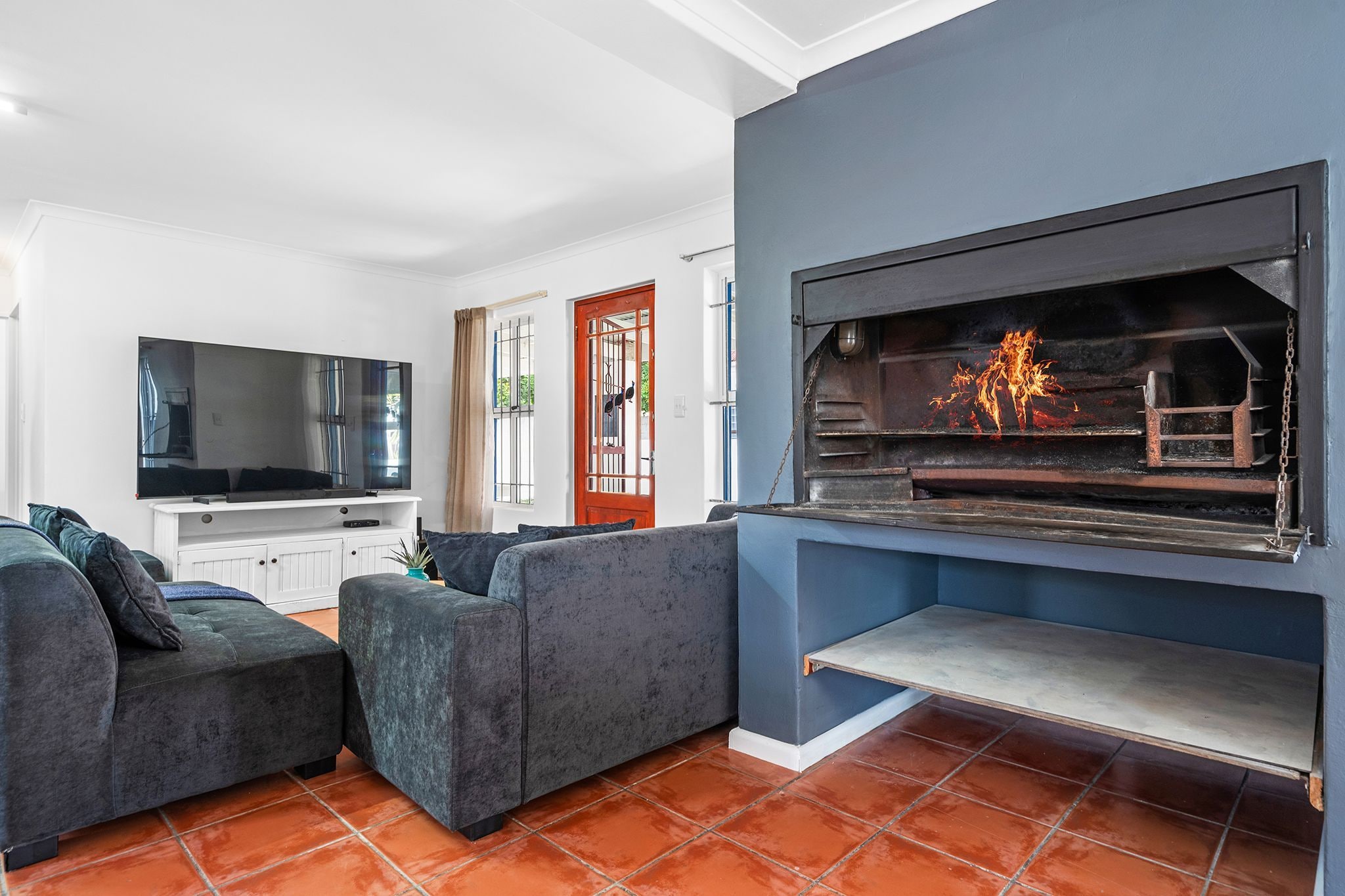 Uma sala de estar com televisão de tela plana, sofás cinzas, lareira e uma porta vermelha.
