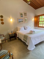 Quarto com cama, cadeira, mesa de cabeceira e obra de arte na parede.