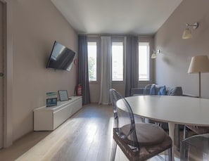 Quarto moderno com televisão de tela plana na parede, mesa de jantar com cadeiras, armário branco pequeno e extintor de incêndio.