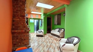 Um quarto com parede de tijolos, uma mesa azul, dois sofás brancos e uma parede verde.