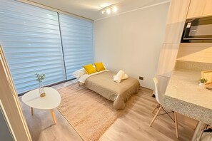 Quarto moderno com cama, mesa de cabeceira e uma pequena janela.
