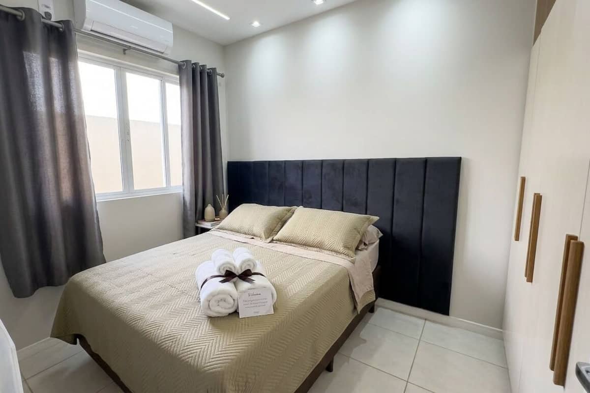 Quarto de hotel com cama, cortinas, janela e mesa de cabeceira.