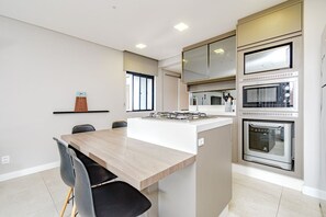 Cozinha moderna com ilha central, fornos embutidos e janela.