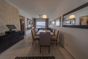Uma sala de jantar com uma mesa comprida, cadeiras, um ventilador de teto e uma janela grande.