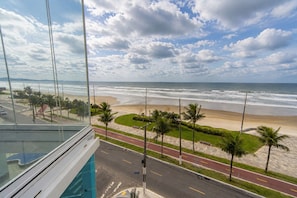 Vista da praia a partir de um arranha-céu, com uma estrada e palmeiras em primeiro plano.