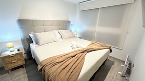 Quarto de hotel moderno com cama, mesas de cabeceira, luminária e janela com persianas.