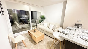 Uma sala de estar moderna com sofá, mesa de centro e área de jantar com cadeiras e uma mesa posta para refeição.