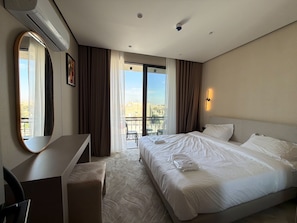 Quarto de hotel com cama, escrivaninha, cadeira, espelho grande e varanda com vista.