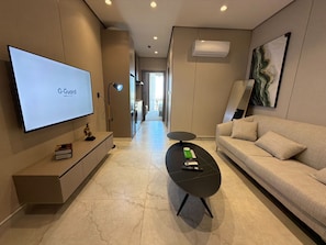 Uma sala de estar moderna com televisão de tela plana, um sofá, uma mesa de centro e um corredor que dá para outro cômodo.
