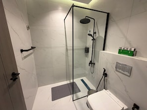 Uma casa de banho moderna com chuveiro em cabine de vidro, sanita e uma pequena prateleira com produtos de higiene pessoal.