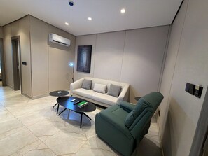 Uma sala de estar moderna com um sofá, uma poltrona verde, uma mesa de centro e um aparelho de ar condicionado na parede.