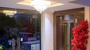 Um lobby moderno com entrada de vidro, um candelabro, um elevador e um arranjo de flores vermelhas.