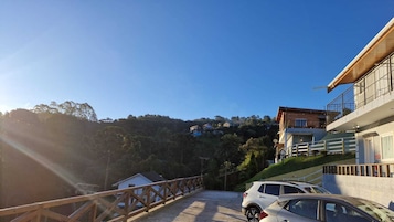 Zona residencial com uma ponte de madeira, um carro branco e um morro com edifícios.