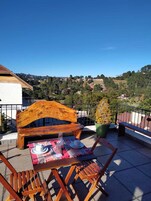 Conjunto de banco e mesa de madeira numa varanda com vista para uma paisagem montanhosa.